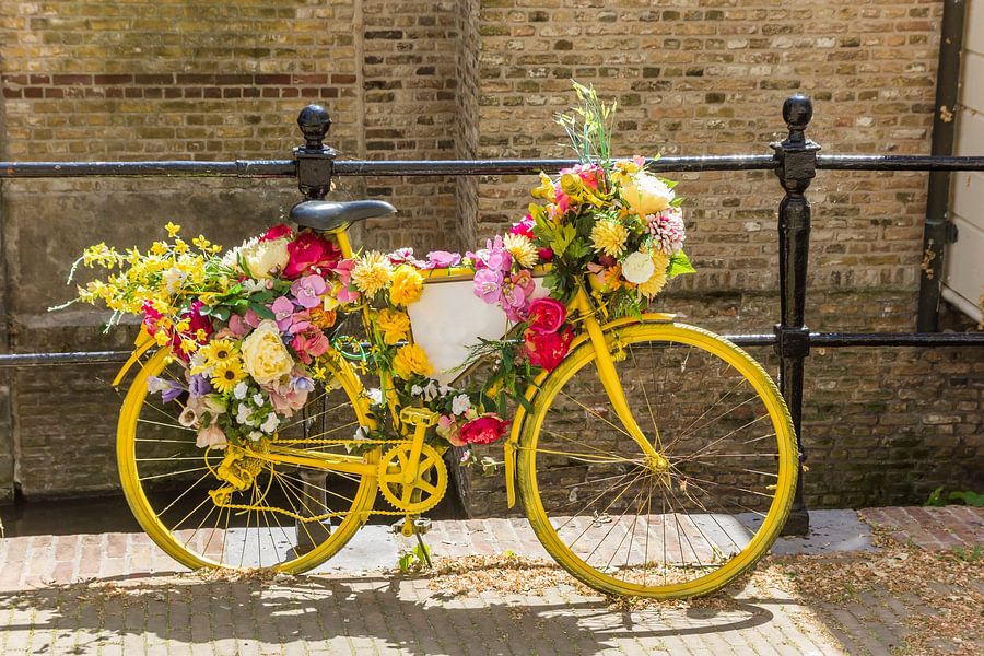 Een oude gele fiets versierd met bloemen staat tegen het hek van een ...