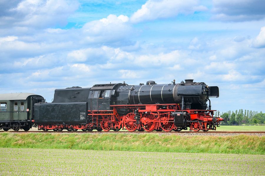 Stoomtrein met zwarte en rode locomotief rijdt op het platteland van ...